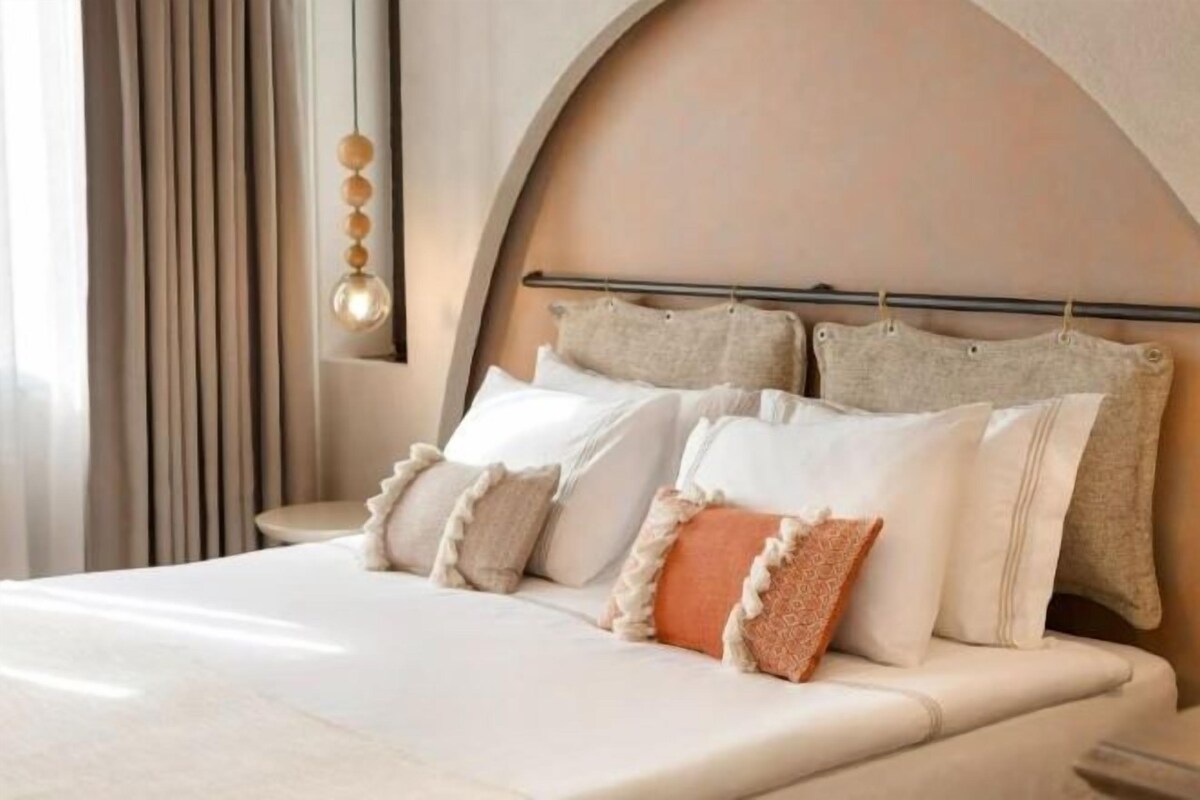 Cama com várias almofadas e cabeceira em quarto com teto arredondado.