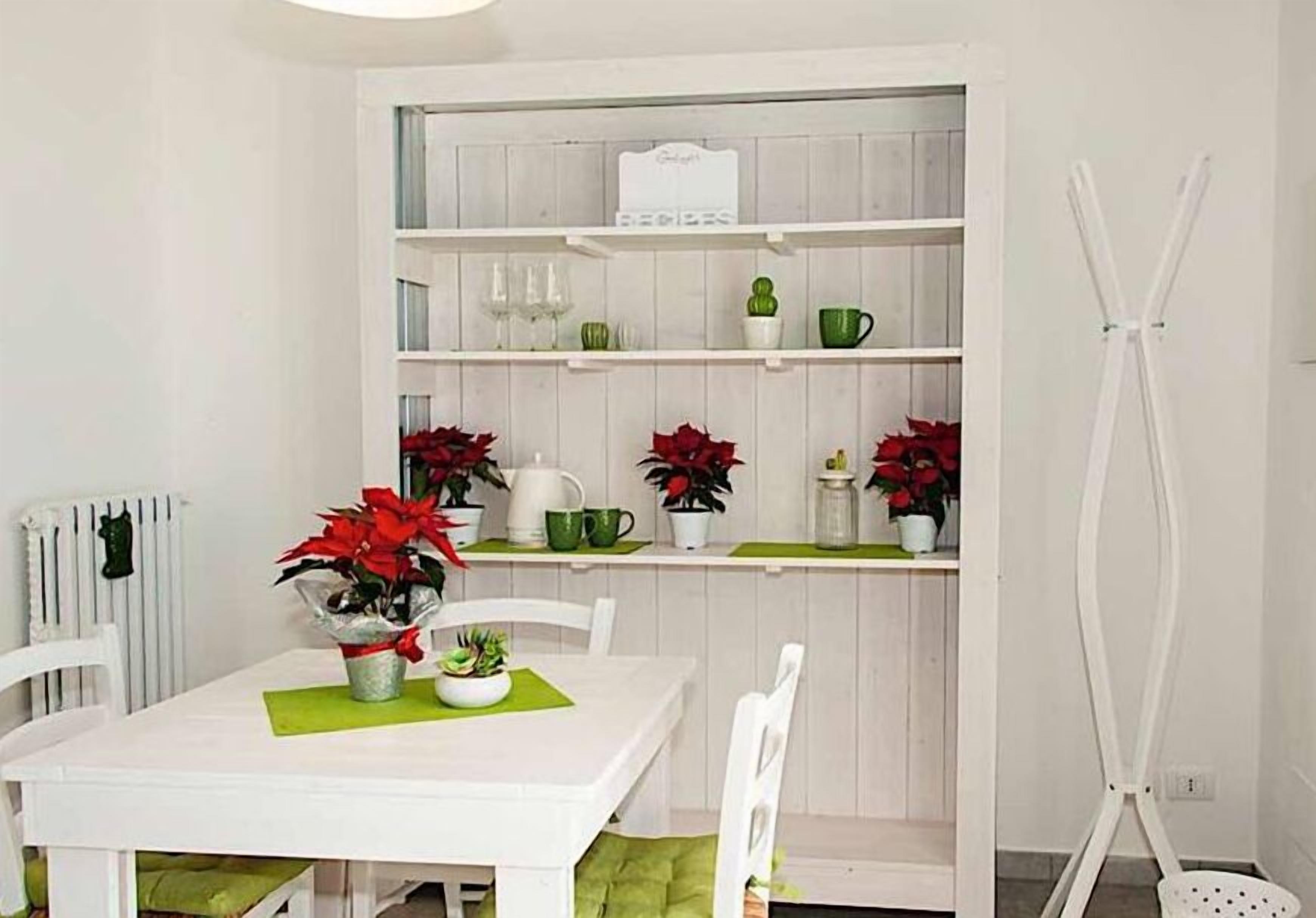 Uma mesa de jantar branca com cadeiras, um armário branco com prateleiras e um radiador branco.