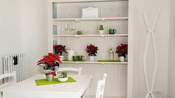 Uma mesa de jantar branca com cadeiras, um armário branco com prateleiras e um radiador branco.