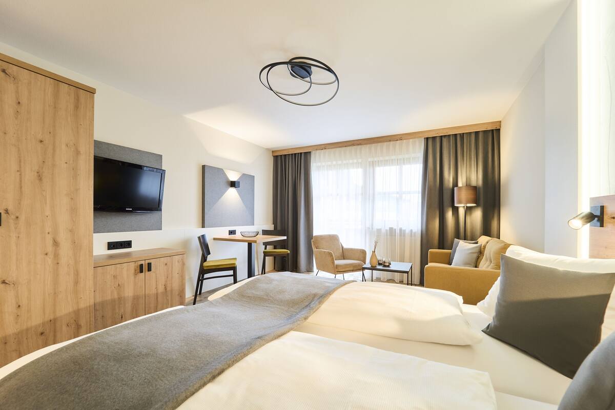 Quarto de hotel com cama, escrivaninha, cadeira, televisão e janela com cortinas.