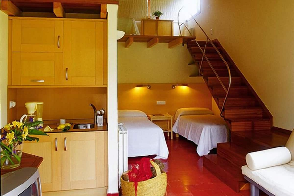 Quarto compacto com cozinha compacta, duas camas, uma mesa pequena e um lance de escadas.