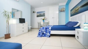 Quarto moderno com cama, mesa de cabeceira, televisão e escrivaninha com cadeiras.