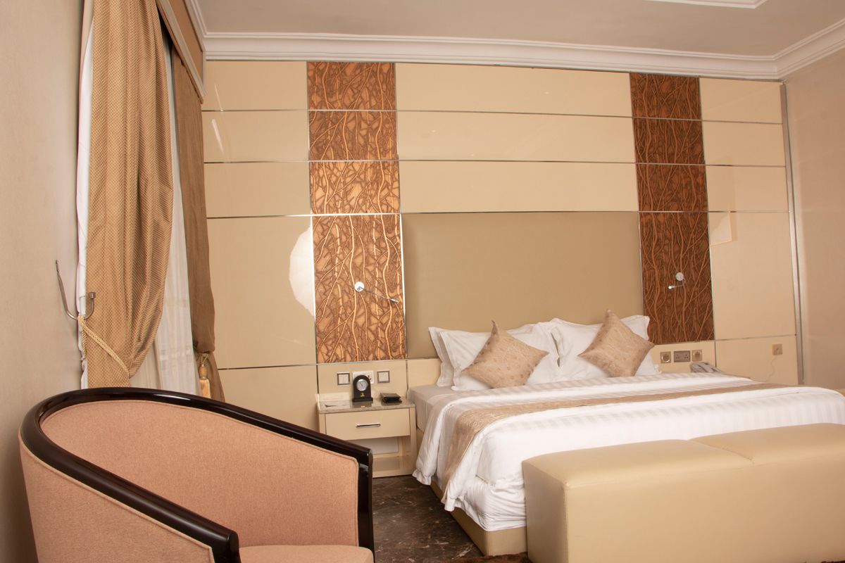 Quarto de hotel com cama, mesas de cabeceira, uma cadeira e um espelho grande.