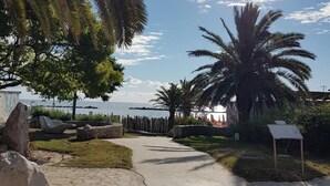 Uma trilha pavimentada que leva a uma área de praia, com palmeiras e vista para o mar.