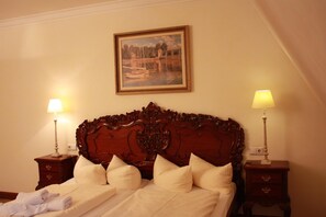 Quarto de hotel com uma cama grande, duas mesas de cabeceira com abajures, um quadro na parede e uma janela com cortinas.