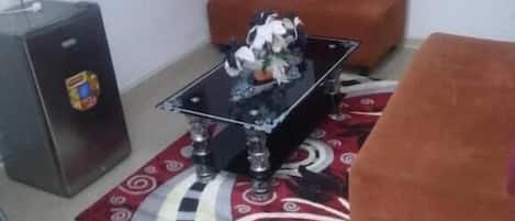 Uma sala de estar com um sofá vermelho, uma mesa de centro com um arranjo floral, um pequeno armário e um tapete estampado.