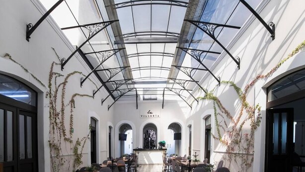 Um restaurante com teto de vidro, mesas, cadeiras e chão de azulejos.