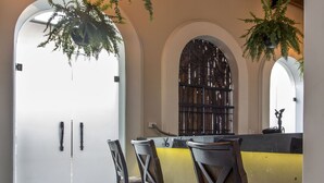 Uma sala de jantar com chão xadrez, cadeiras de madeira, um balcão e teto com vigas aparentes.