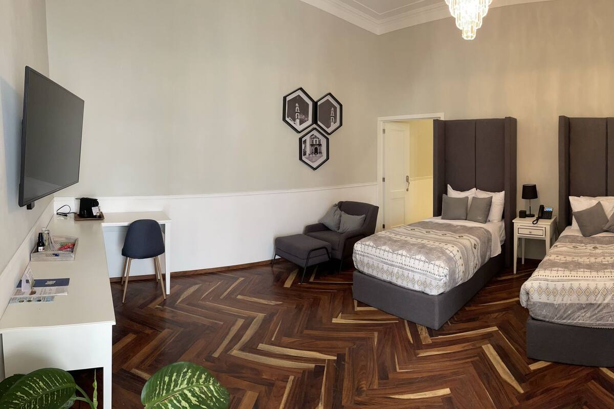 Quarto de hotel com duas camas, uma escrivaninha, uma cadeira e uma televisão.