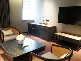 Quarto de hotel com sofá, mesa de jantar, televisão, escrivaninha e lixeira.