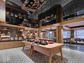 Um restaurante moderno com uma mesa de madeira central, luminárias pendentes e ladrilhos no chão com padrão.
