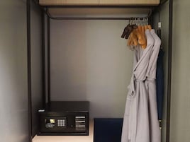 Quarto compacto com micro-ondas sobre uma mesinha, roupão pendurado e cabide de madeira.