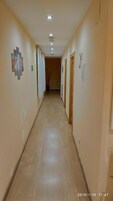 Um corredor com piso de madeira, paredes bege e luminárias no teto.