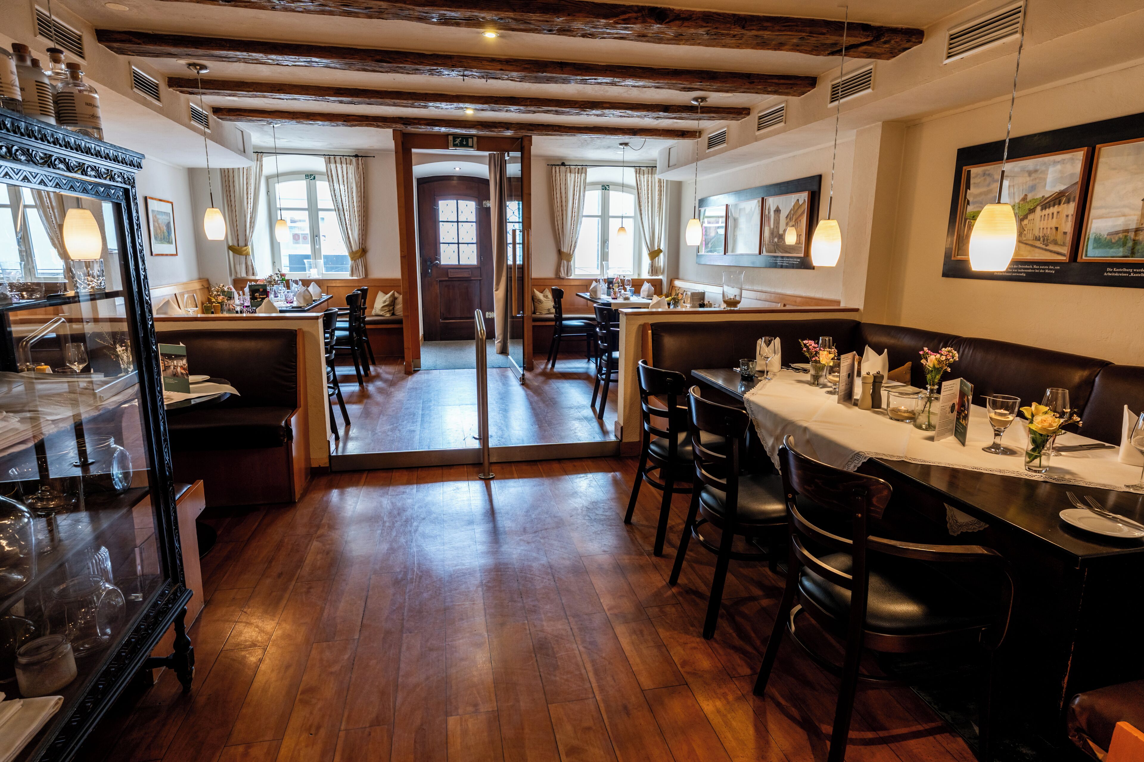 Restaurante com pisos de madeira, assentos de cabine em couro escuro e uma mesa de jantar central decorada com toalhas brancas e velas.