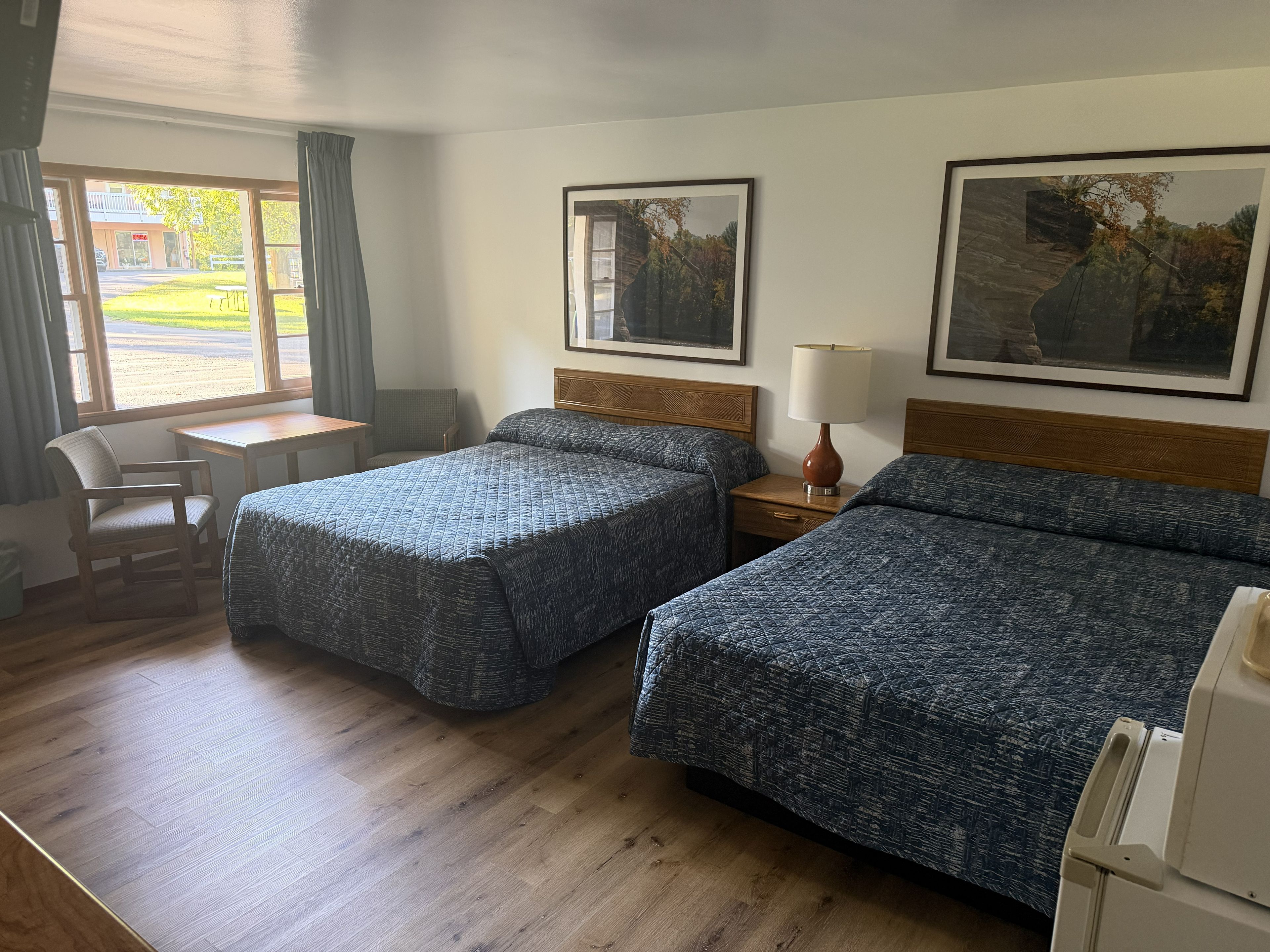 Quarto de hotel com duas camas, uma escrivaninha, uma cadeira e uma janela com cortinas.