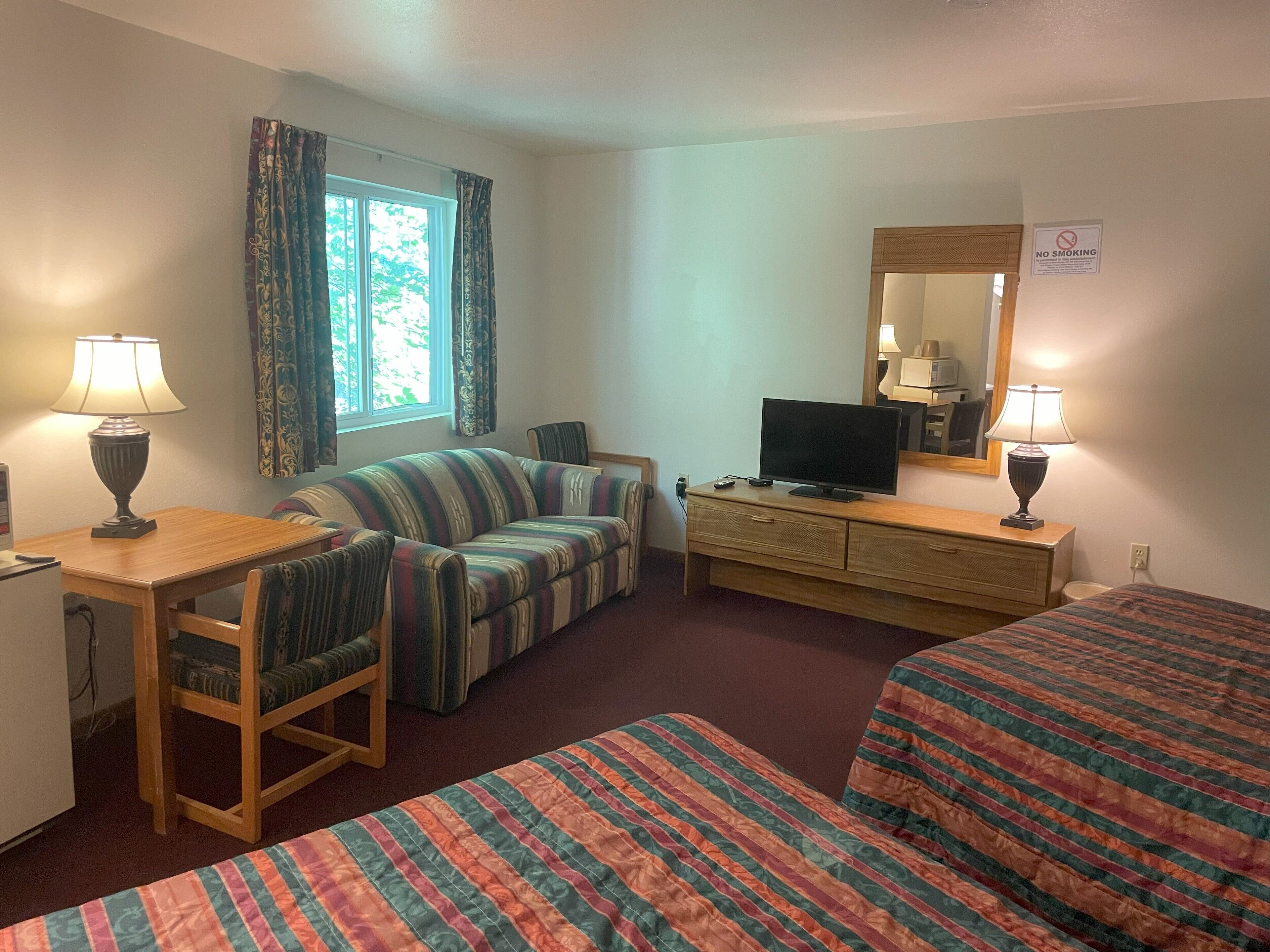 Quarto de hotel com sofá, televisão, escrivaninha com luminária e cama.