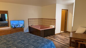 Quarto de hotel com uma cama grande, banheira, escrivaninha de madeira, televisão e vista para a cidade.