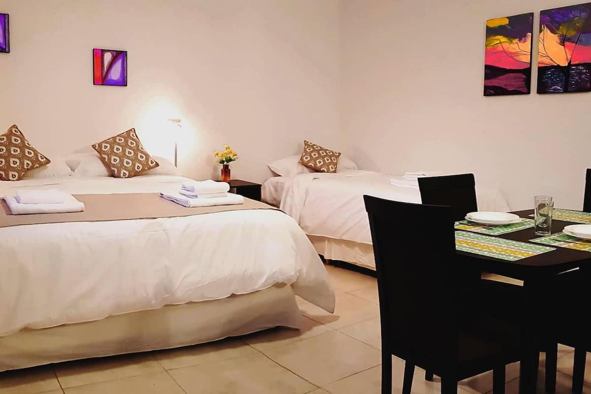 Quarto de hotel com duas camas, uma mesa de jantar e cadeiras, e obras de arte nas paredes.