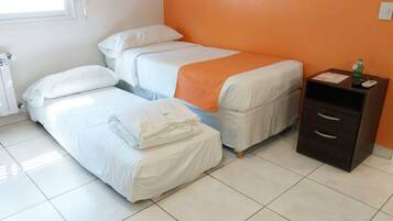 Quarto de hotel com duas camas, uma mesa de cabeceira e uma pequena mesa com uma garrafa.