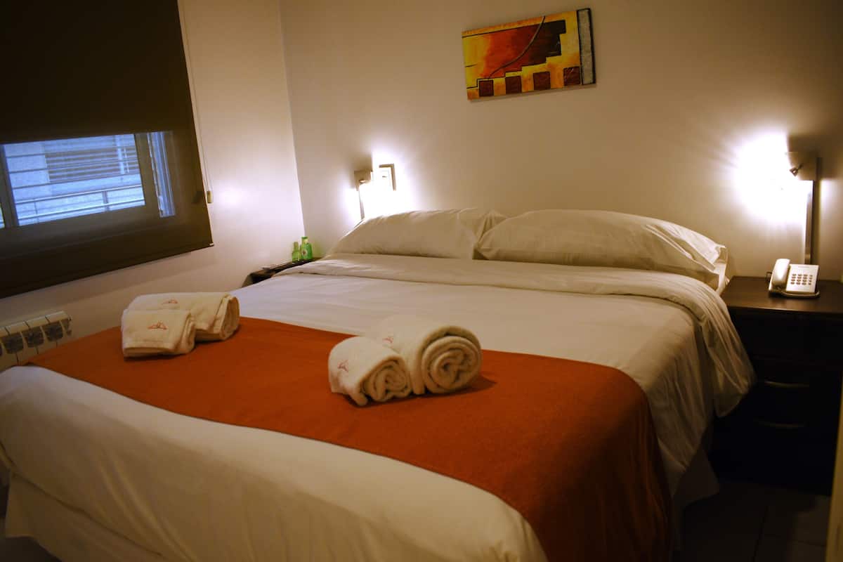 Quarto de hotel com cama grande, duas almofadas, mesa de cabeceira com telefone e um quadro na parede.