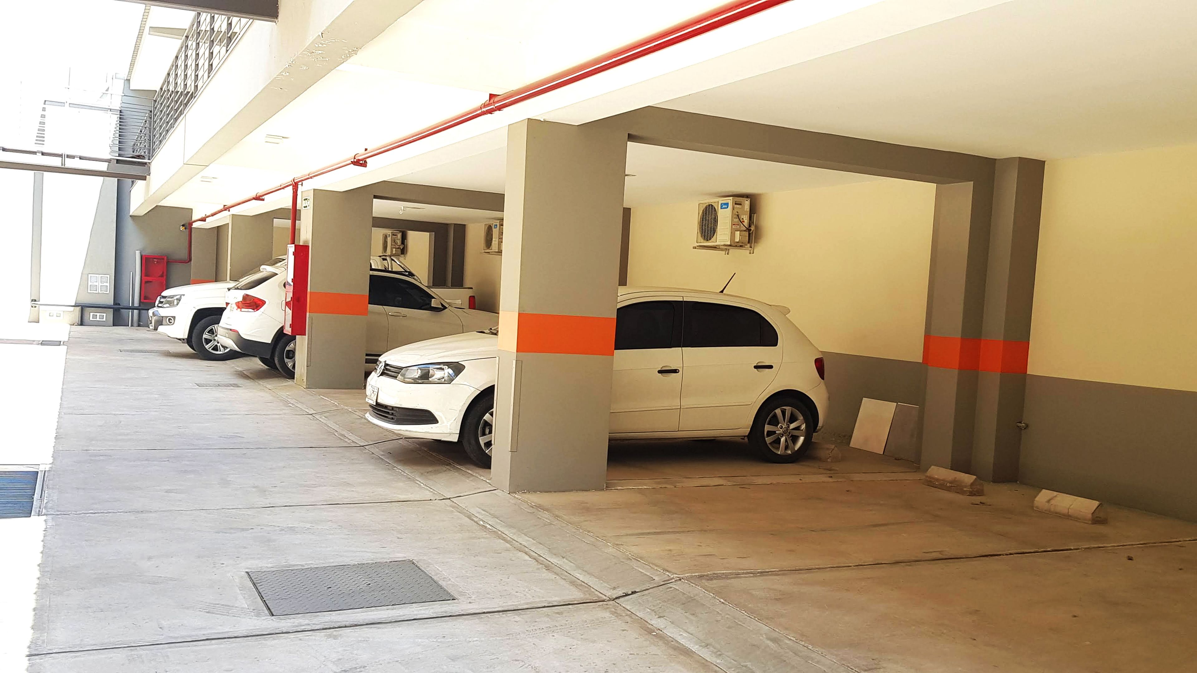 Uma área de estacionamento coberta com vários carros estacionados sob um teto, piso de concreto e colunas estruturais visíveis.