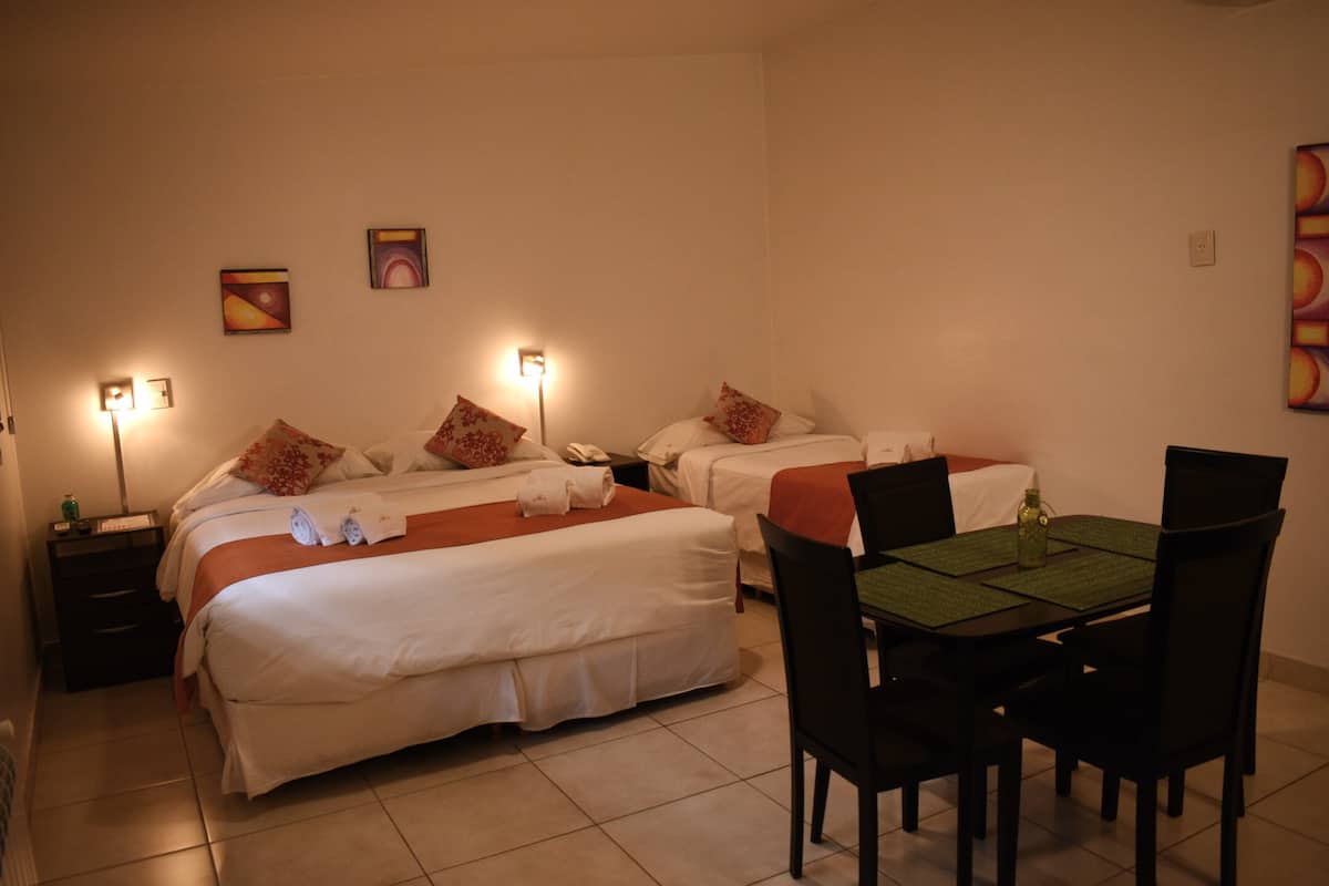 Quarto de hotel com duas camas, uma mesa de jantar com cadeiras e obras de arte nas paredes.