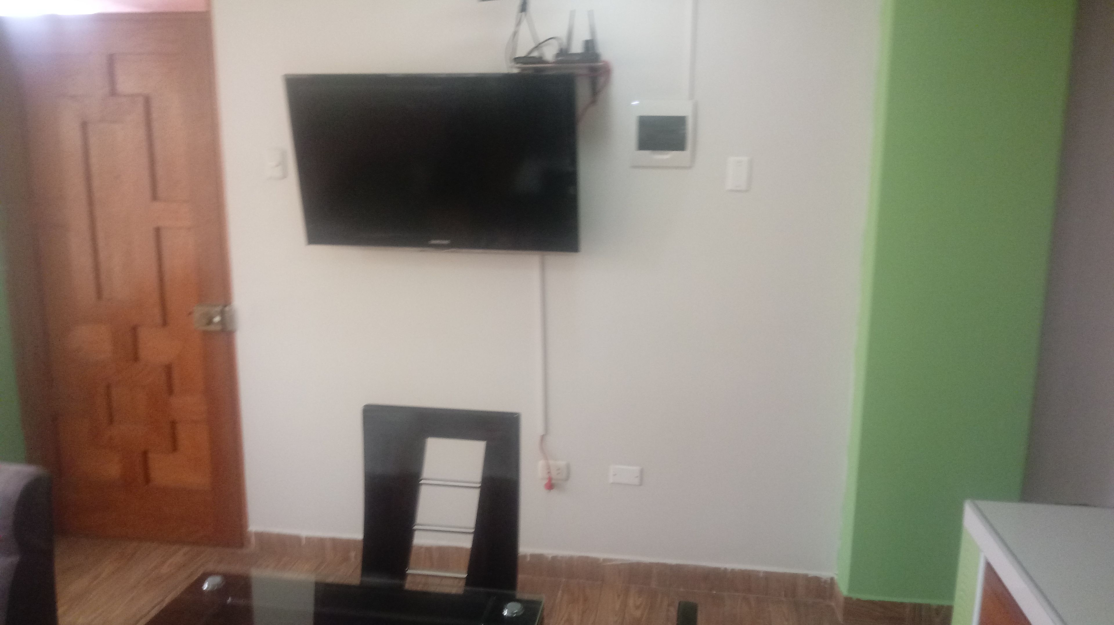 Quarto com televisão na parede, porta de madeira e uma cadeira.