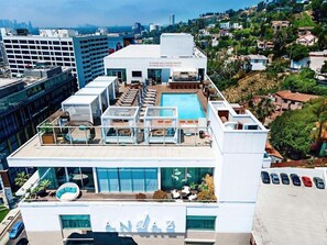 Área de piscina no terraço, com espreguiçadeiras e piscina, cercada por edifícios modernos e vegetação.