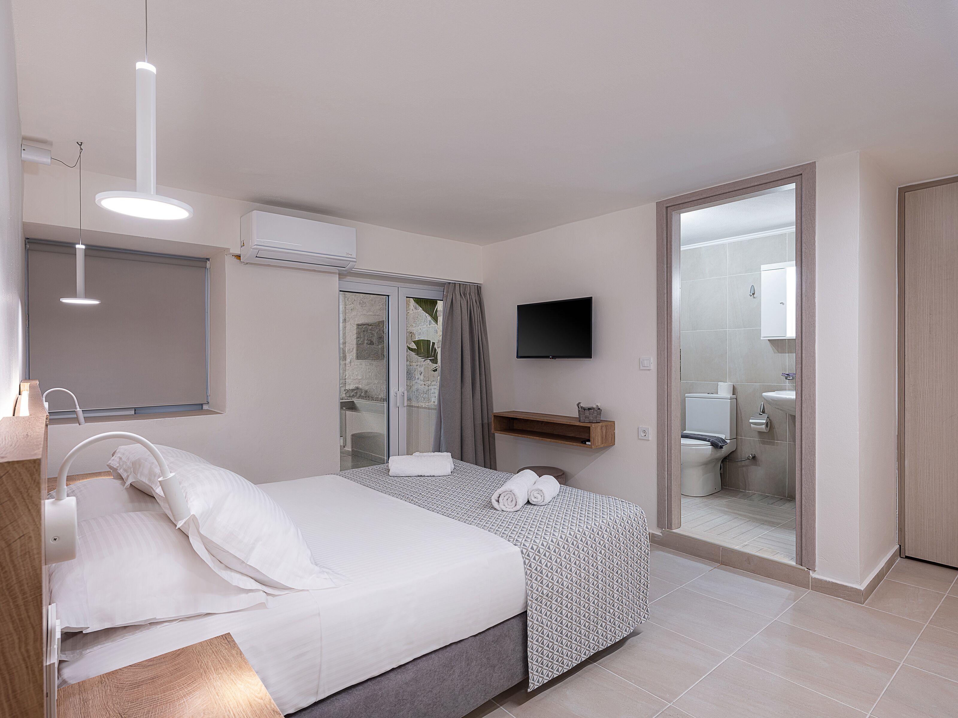 Quarto de hotel moderno com cama, televisão, banheiro e porta de vidro deslizante para a varanda.