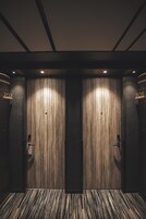 Um par de portas duplas de madeira com um número sobre cada porta, em um corredor com iluminação fraca e carpete estampado.
