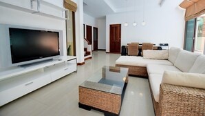 Uma sala de estar moderna com televisão de tela plana, mesa de centro de vime e um sofá.