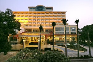 Um hotel de vários andares com uma entrada imponente, palmeiras e fachada bem iluminada.