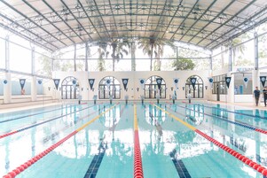 Piscina interna com pistas demarcadas, teto coberto e posto de salva-vidas.