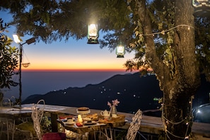 Mesa posta ao ar livre com vista para o pôr do sol, lanternas e luzes de Natal.