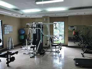 Uma academia com diversos equipamentos de exercício, um espelho grande e uma janela com vista para áreas verdes.
