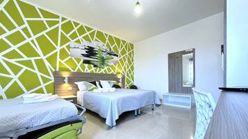 Quarto de hotel com duas camas, design geométrico verde na parede, um espelho grande e uma escrivaninha com um laptop.