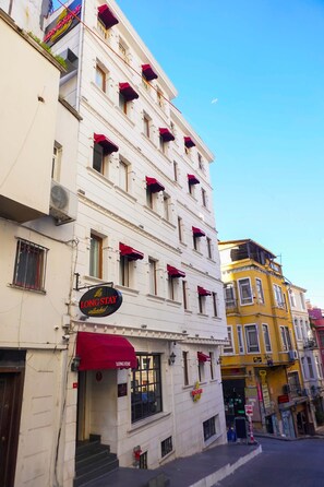 Um edifício de vários andares com um letreiro de hotel 'Long Stay', toldos vermelhos e um céu azul claro.