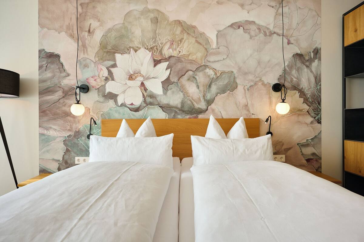 Cama de casal com lençóis brancos, cabeceira de madeira e duas luminárias de leitura fixadas na parede.