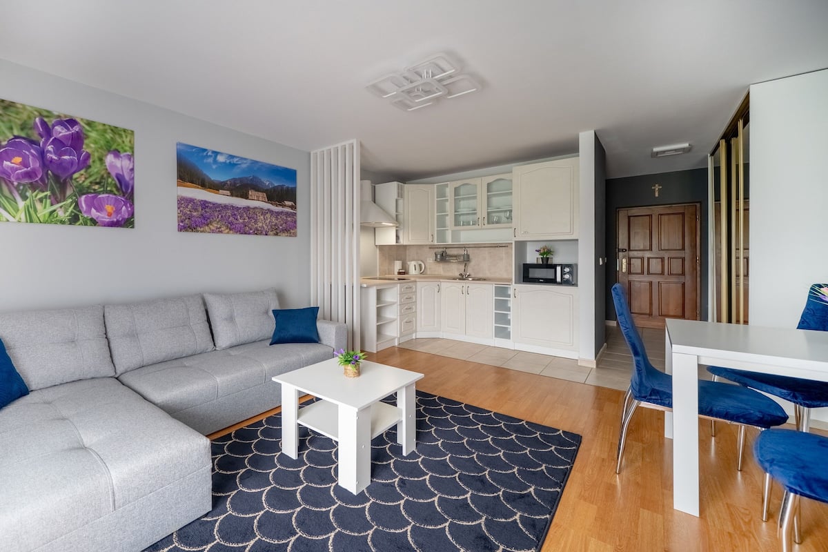 Uma sala de estar moderna com um sofá cinza, uma mesinha branca e um tapete azul estampado.