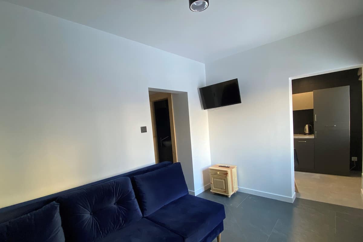Uma sala de estar moderna com um sofá azul escuro, uma televisão de tela plana na parede e um pequeno armário de madeira.