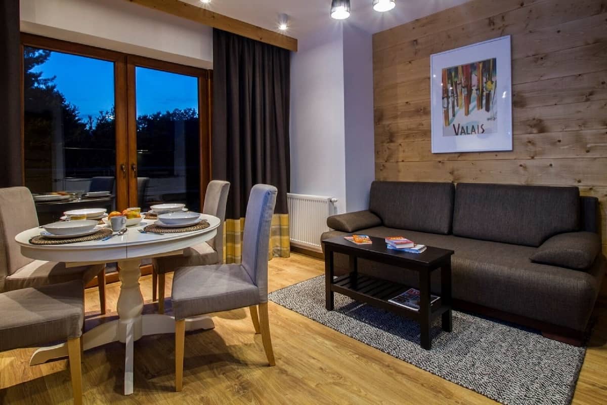 Uma sala de estar moderna com uma mesa de jantar redonda, sofás cinzas e uma parede de destaque em madeira.