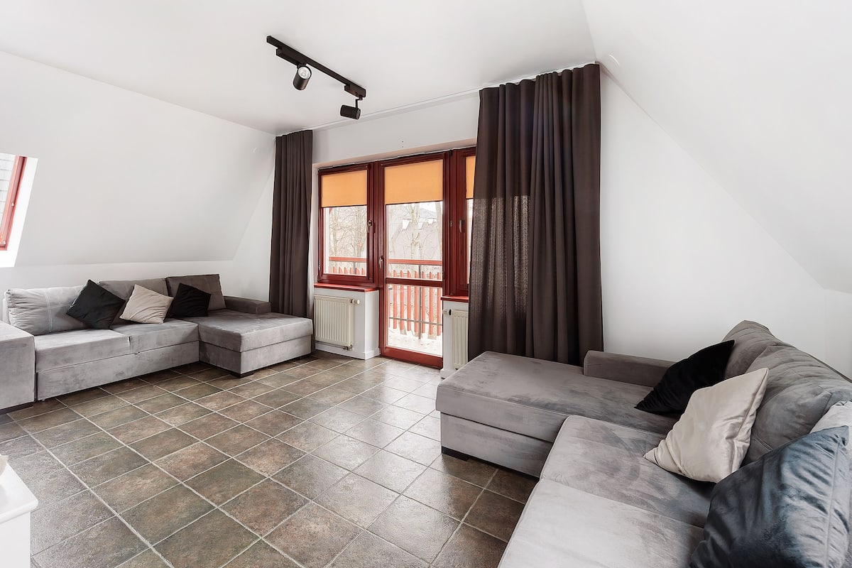 Uma sala de estar moderna com um sofá seccional, uma mesinha com um urso de pelúcia e uma janela com cortinas.