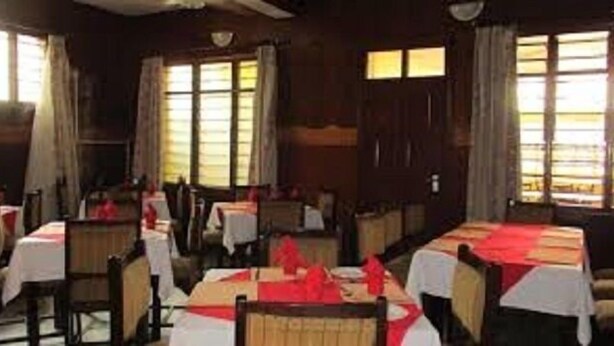 Um restaurante com várias mesas, cada uma coberta por toalhas brancas e guardanapos vermelhos.