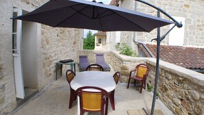 Um edifício de pedra com um pátio que inclui uma mesa, cadeiras, um guarda-sol e uma pequena mesa.