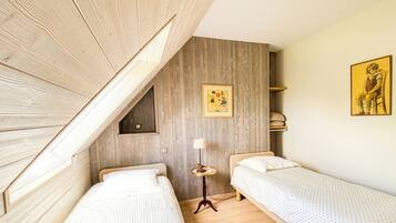 Quarto com duas camas de solteiro, paredes de madeira, uma mesa redonda pequena com abajur e um quadro na parede.