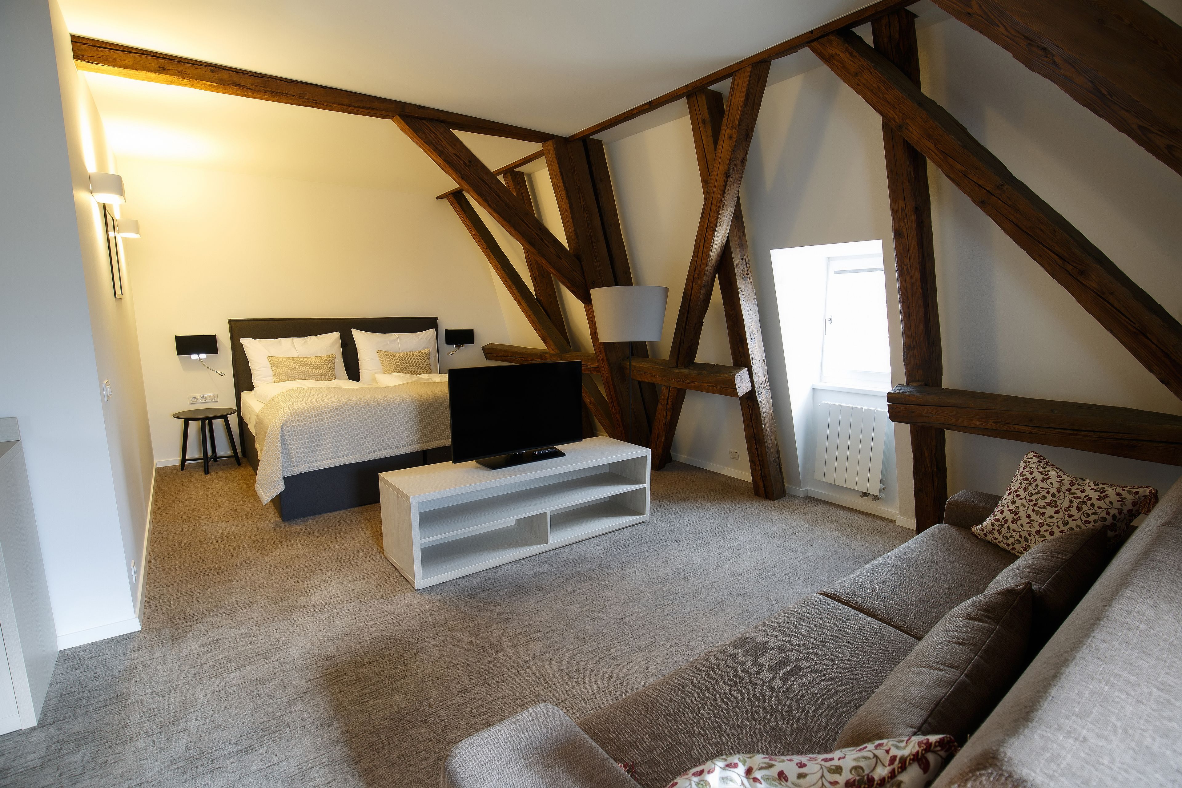 Quarto com cama, televisão, sofá e estrutura de teto em madeira.