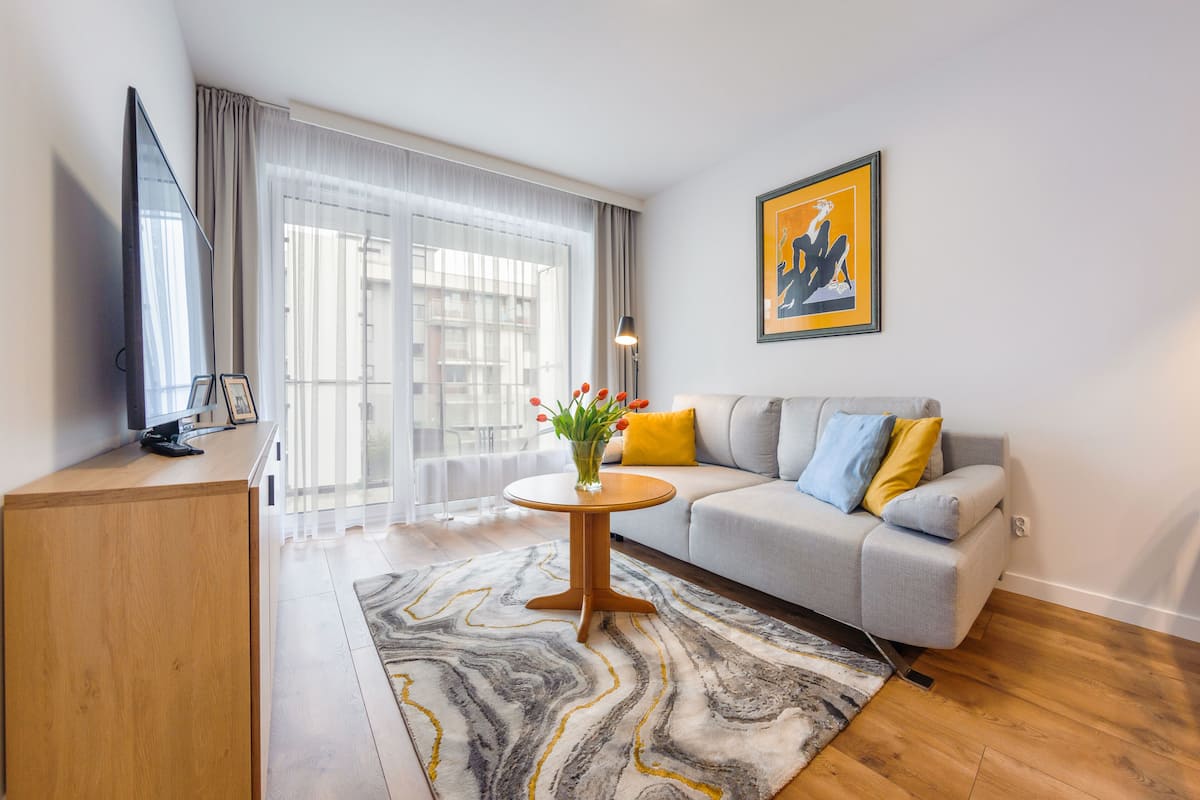 Uma sala de estar moderna com um sofá cinzento, uma mesa de centro de madeira e uma TV de tela plana sobre um armário de madeira.
