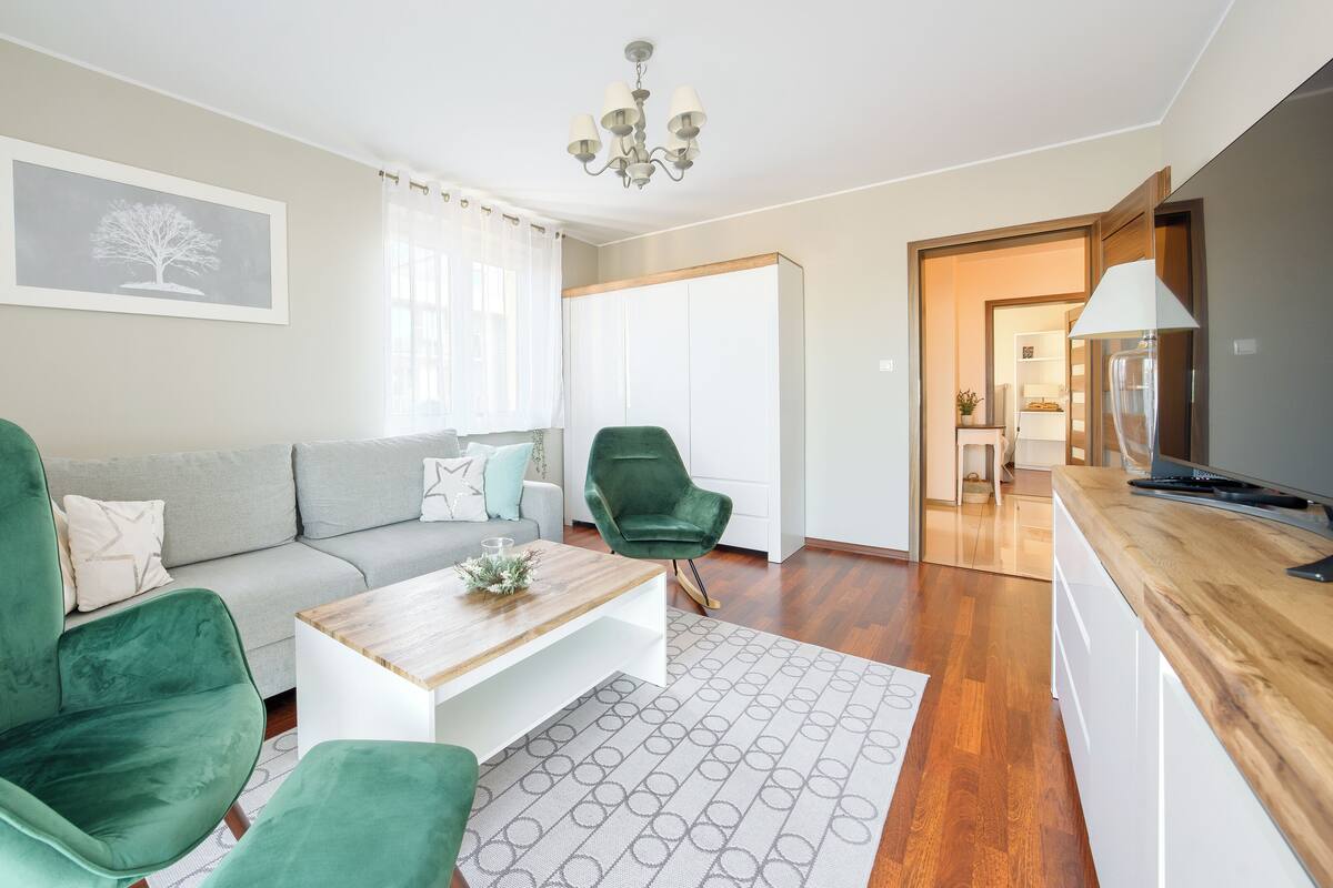 Uma sala de estar moderna com um sofá cinzento, poltronas verdes, uma mesa de centro de madeira e um candelabro.