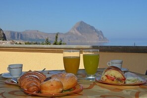 Mesa com croissants, um sanduíche e duas chávenas de chá, com vista para uma paisagem montanhosa.