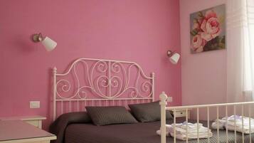 Quarto decorado em tons de rosa, com estrutura de cama de metal, roupa de cama escura e mesa de cabeceira com toalhas.